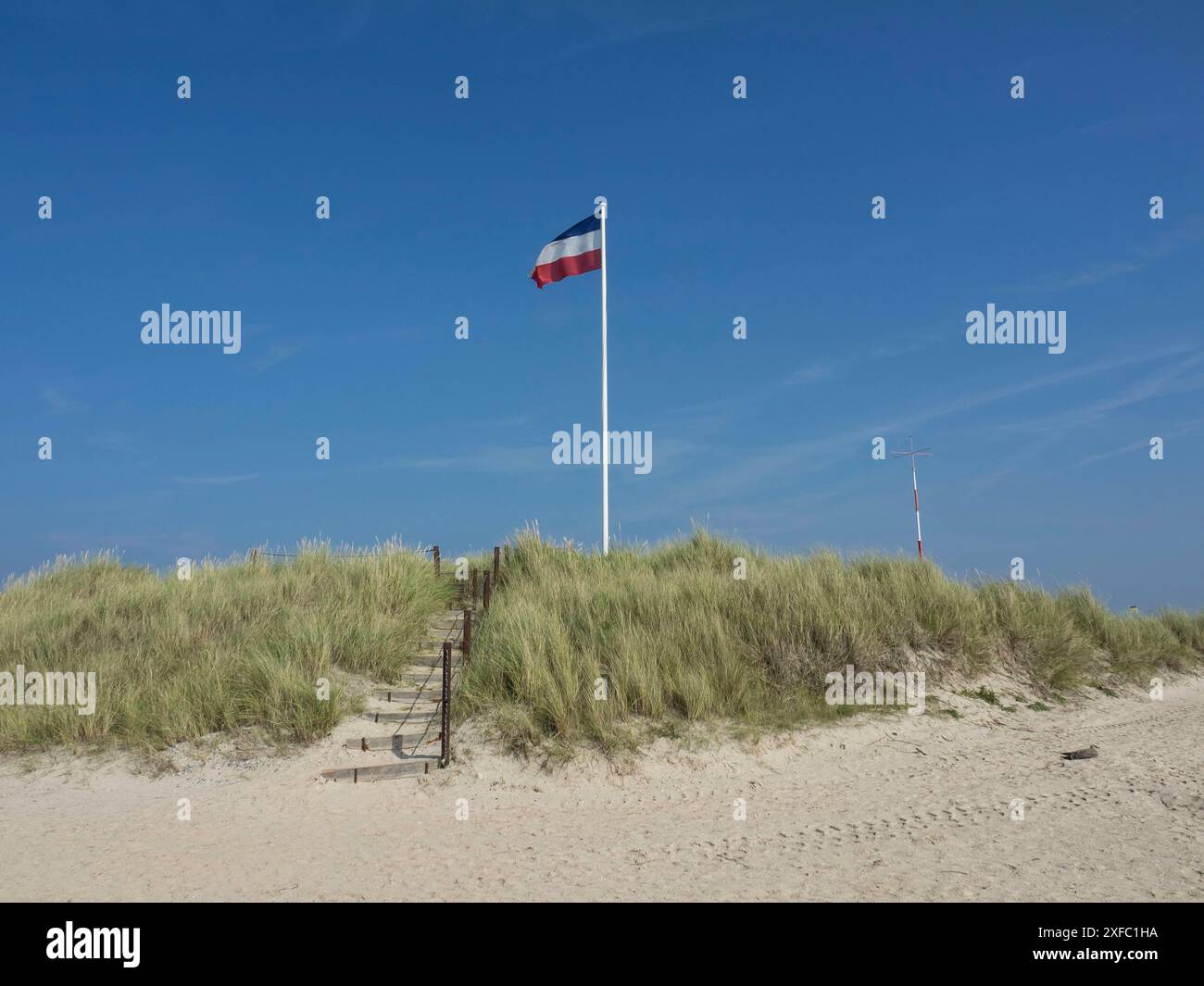 A flag waves in the wind on a sandy dune under a clear blue sky, helgoland, north sea, germany ...