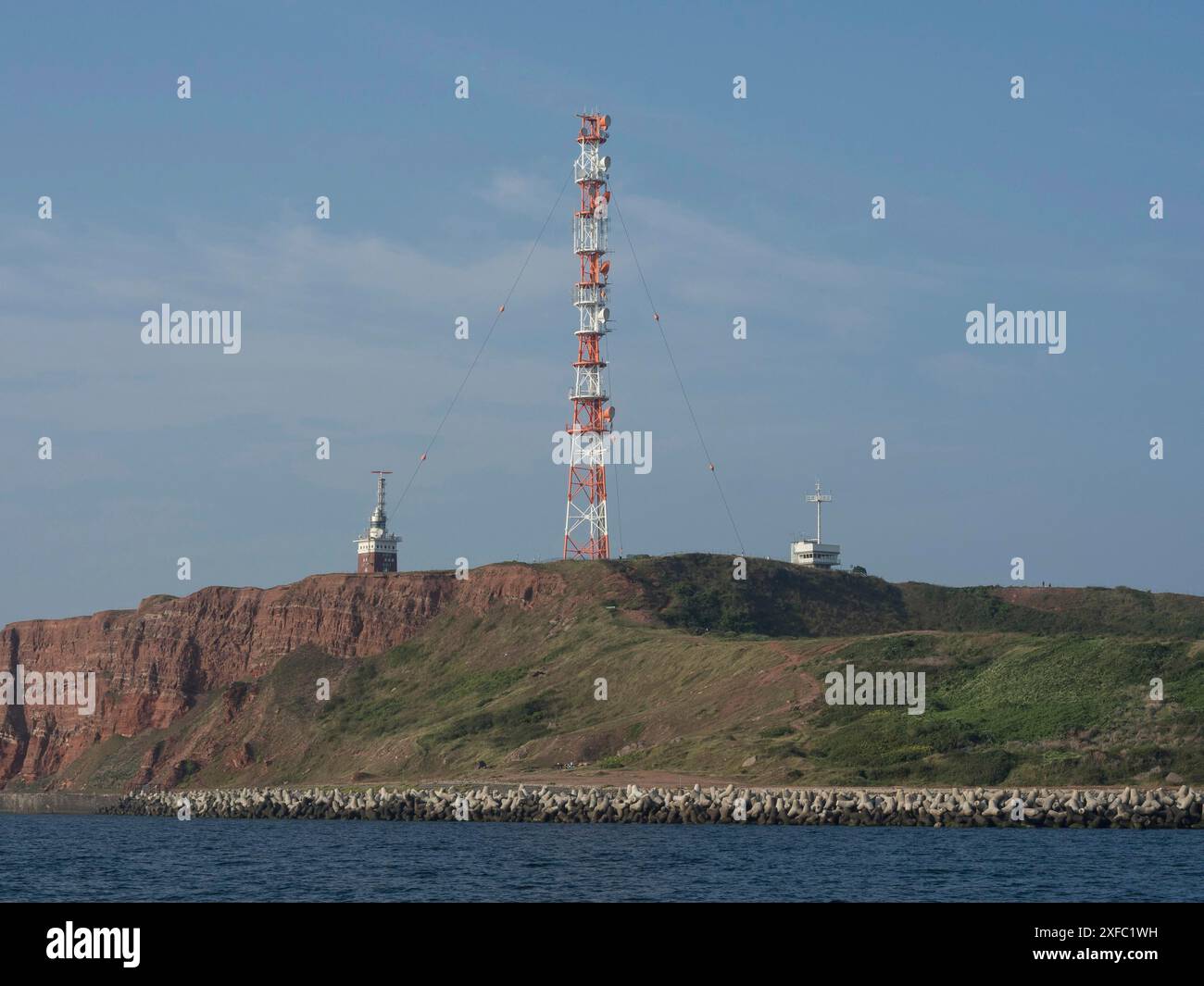 A transmission mast on a rocky coast next to the sea under a clear blue sky, helgoland, north ...