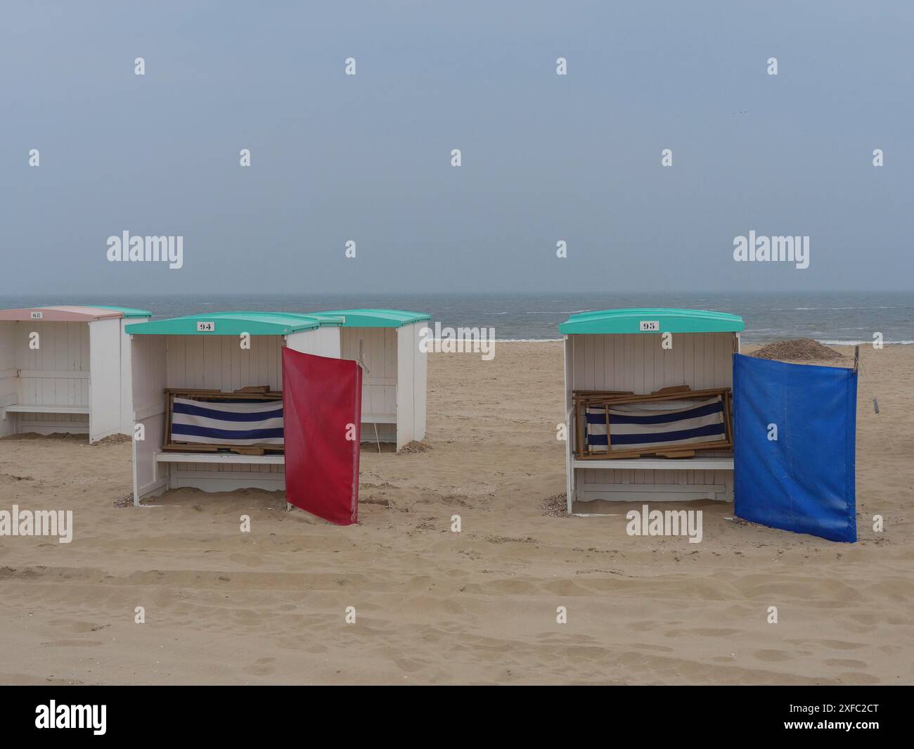 Two beach chairs on the beach, one with a red, the other with a blue ...