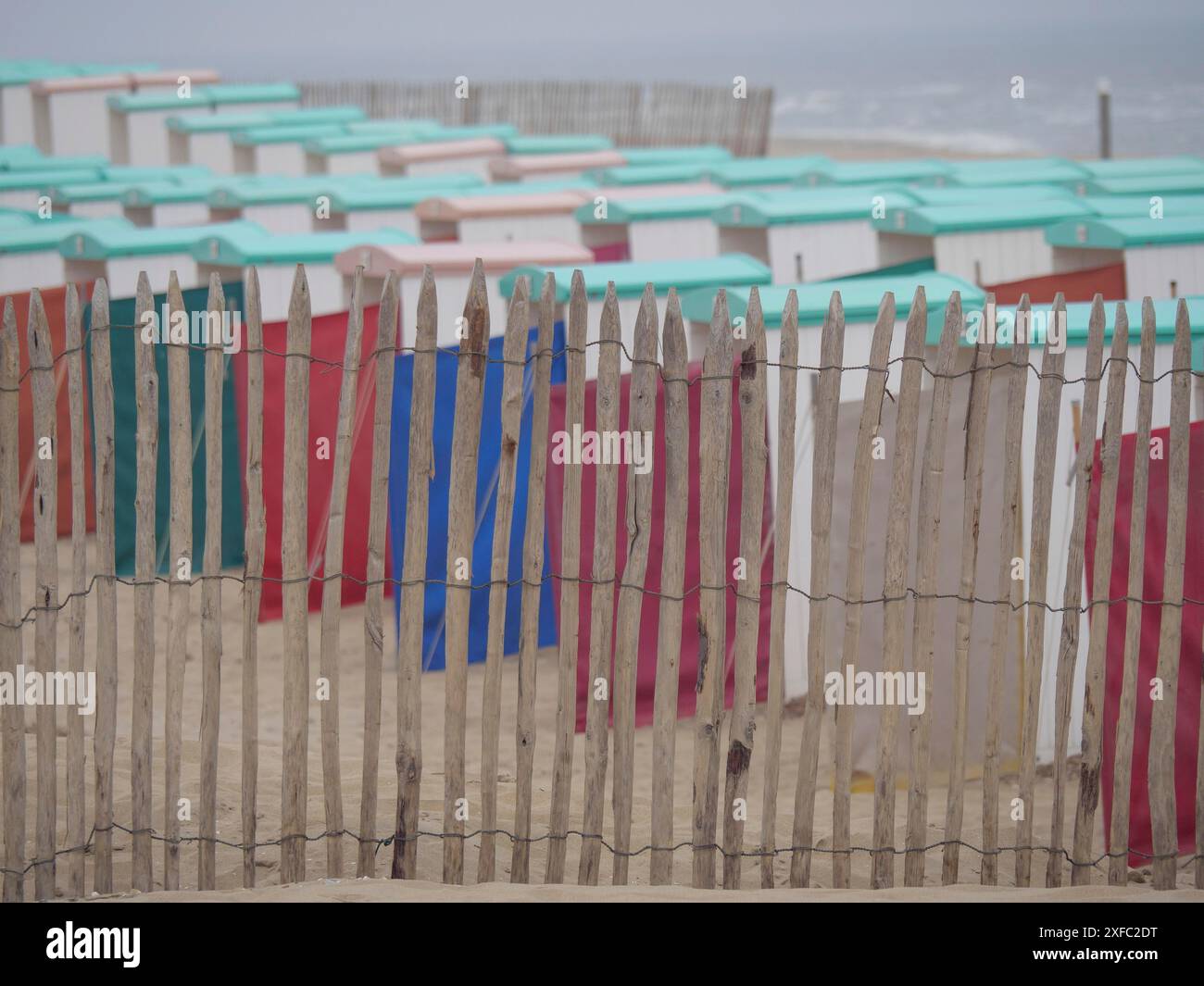 Colourful rags hanging from a fence in front of rows of beach huts by ...
