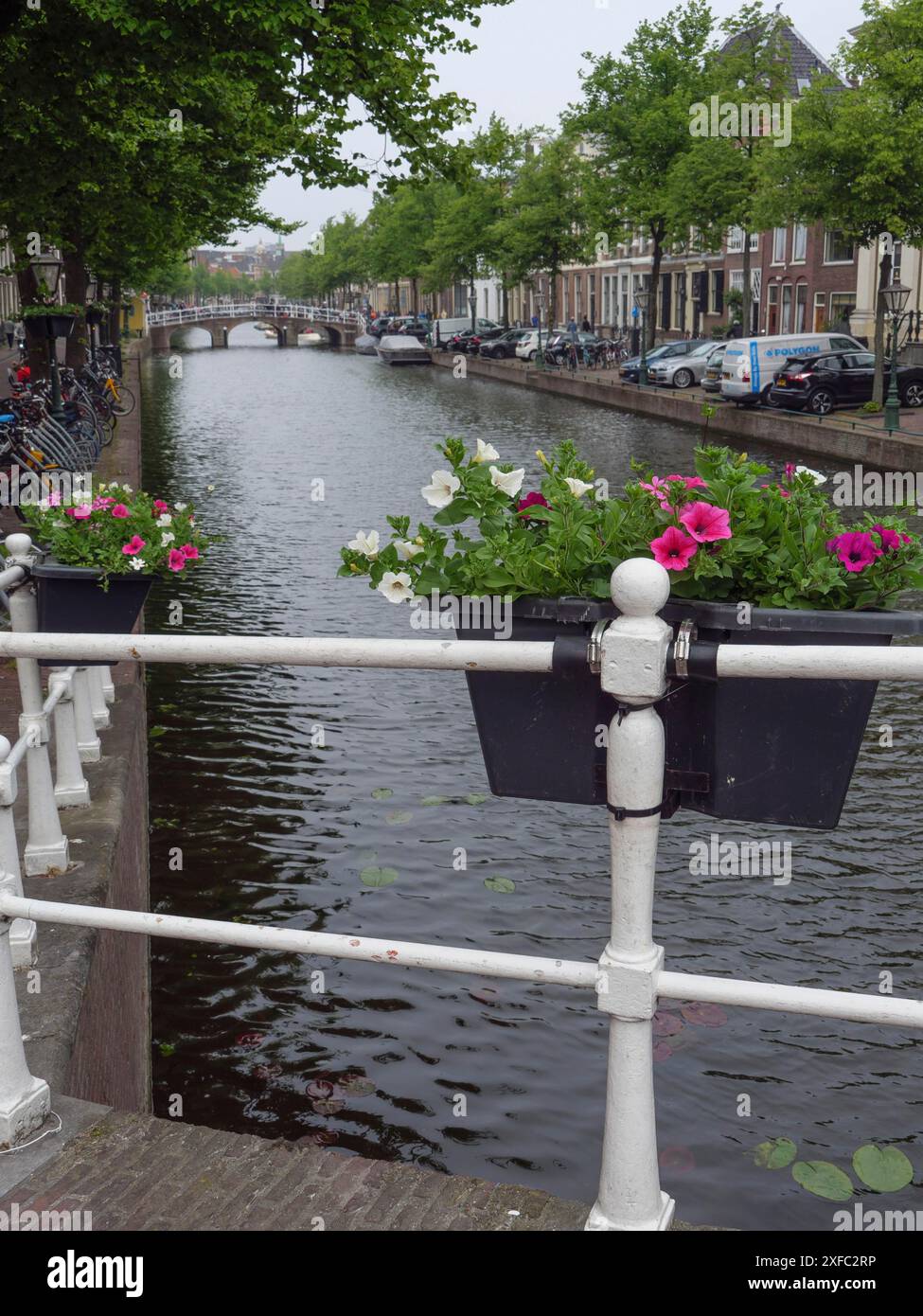 Flower boxes on a bridge railing over a canal with boats and urban ...