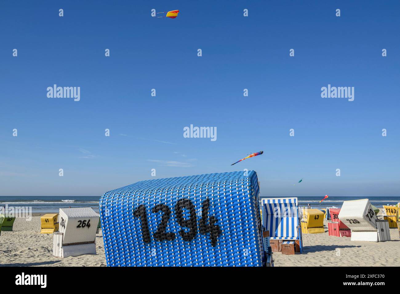 Colourful beach chairs stand on the beach under a blue sky with flying ...