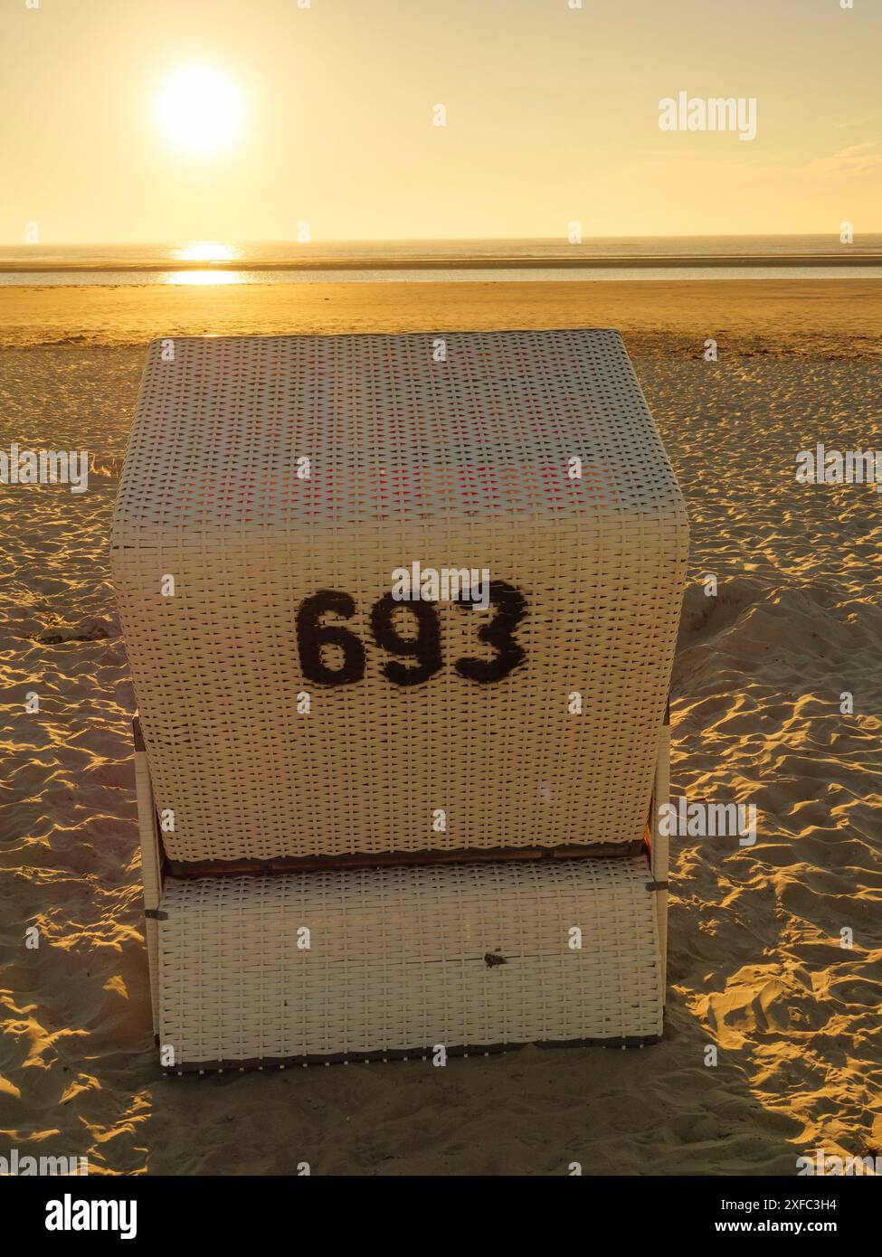 A single beach chair with the number 693 on the beach during a sunset ...