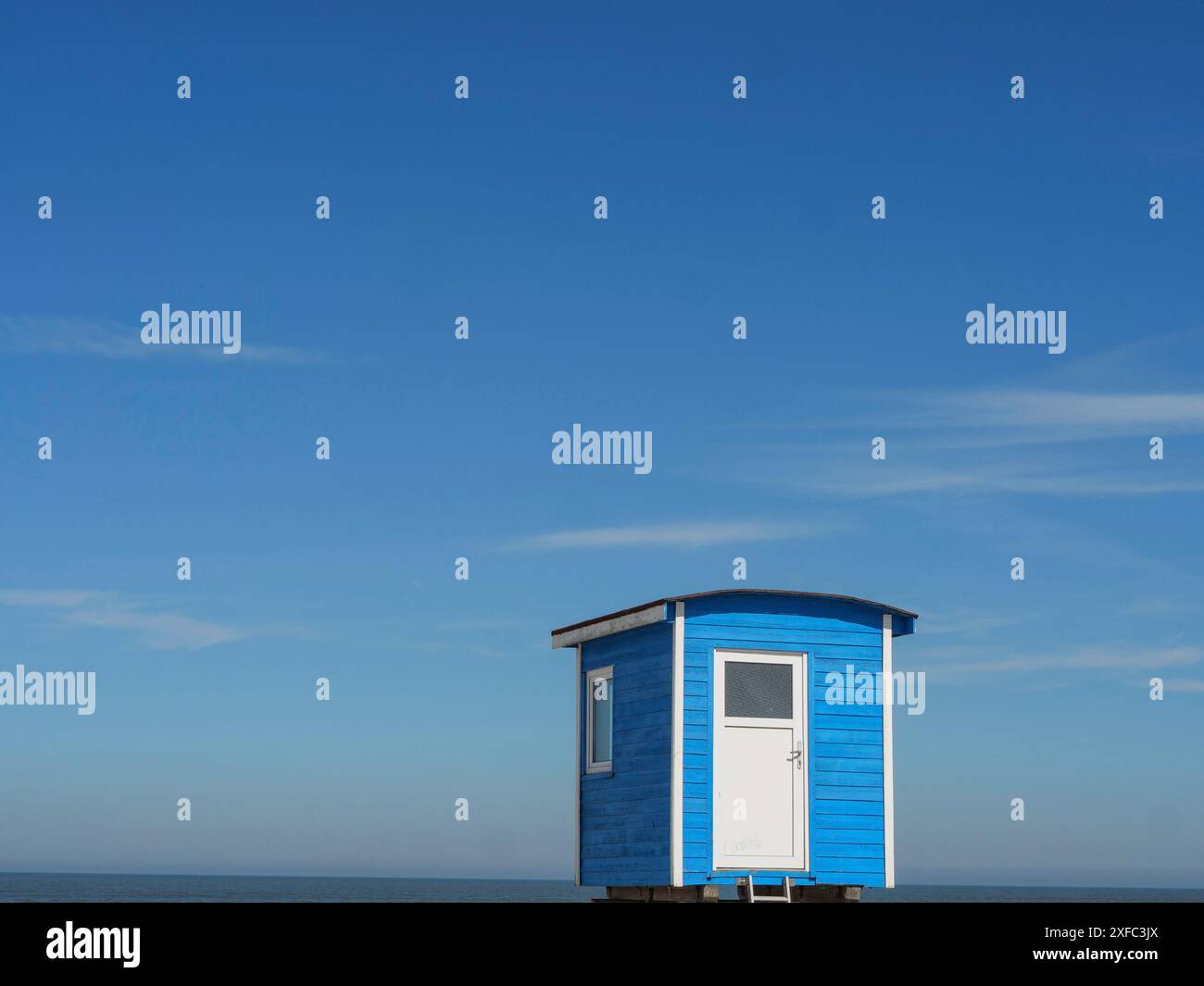 A simple blue wooden hut on the beach in front of a wide blue sky ...