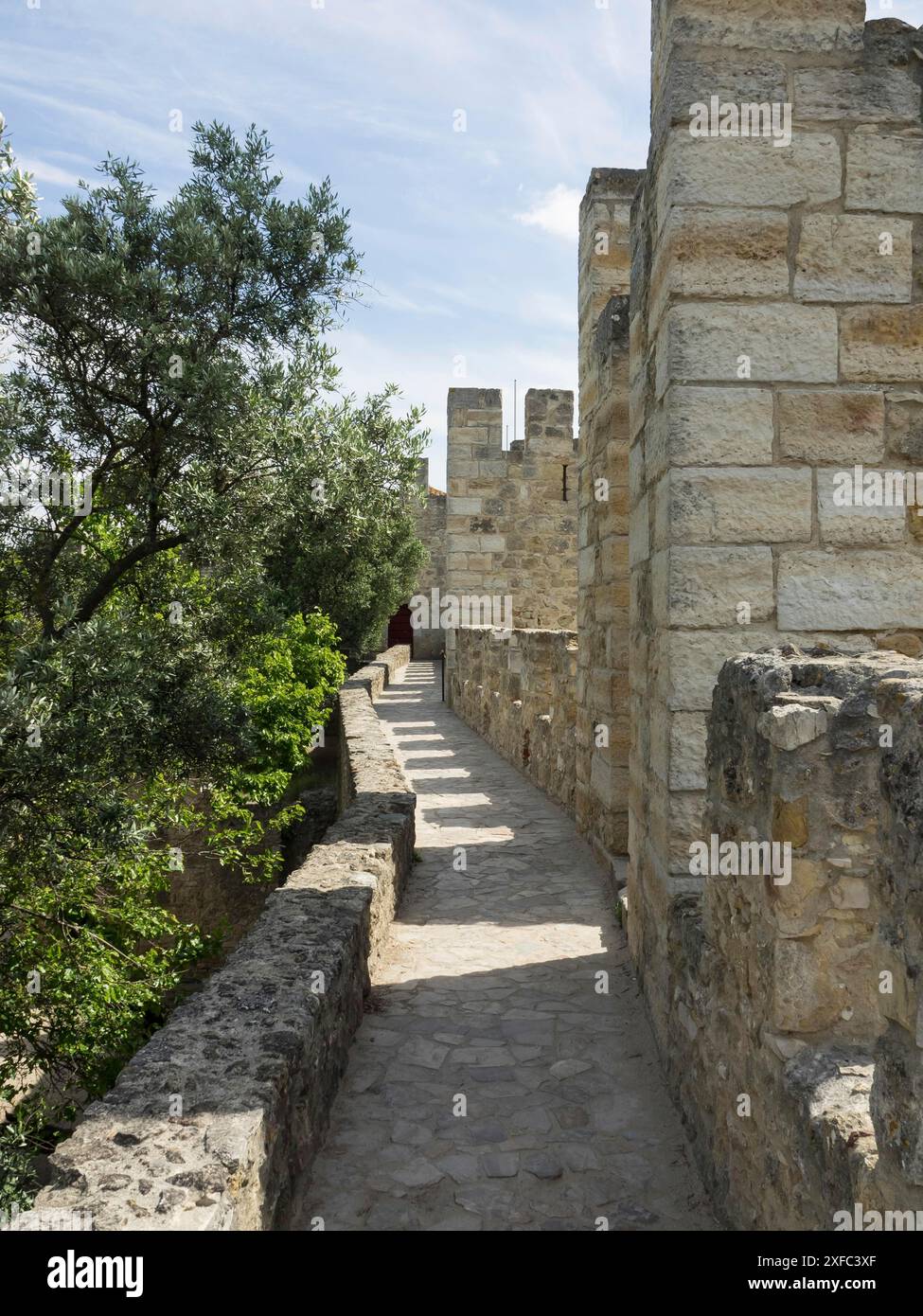 A narrow path runs along the old castle wall, flanked by trees and ...