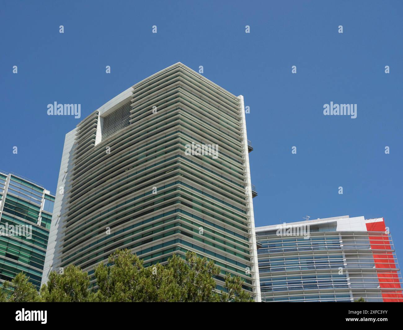 Modern tall building with glass facade and green trees in front under a ...