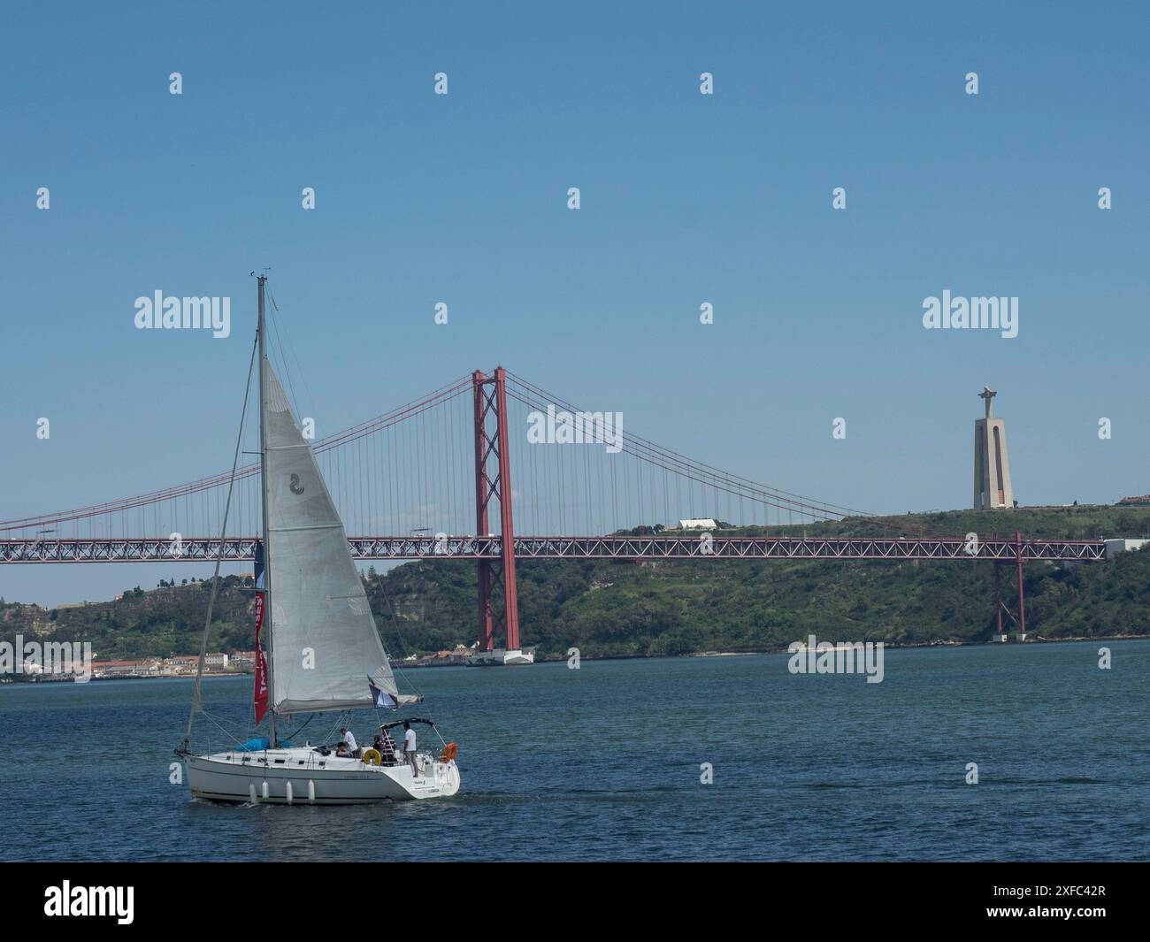 Sailing boat on a river with a big red bridge and statue in the ...