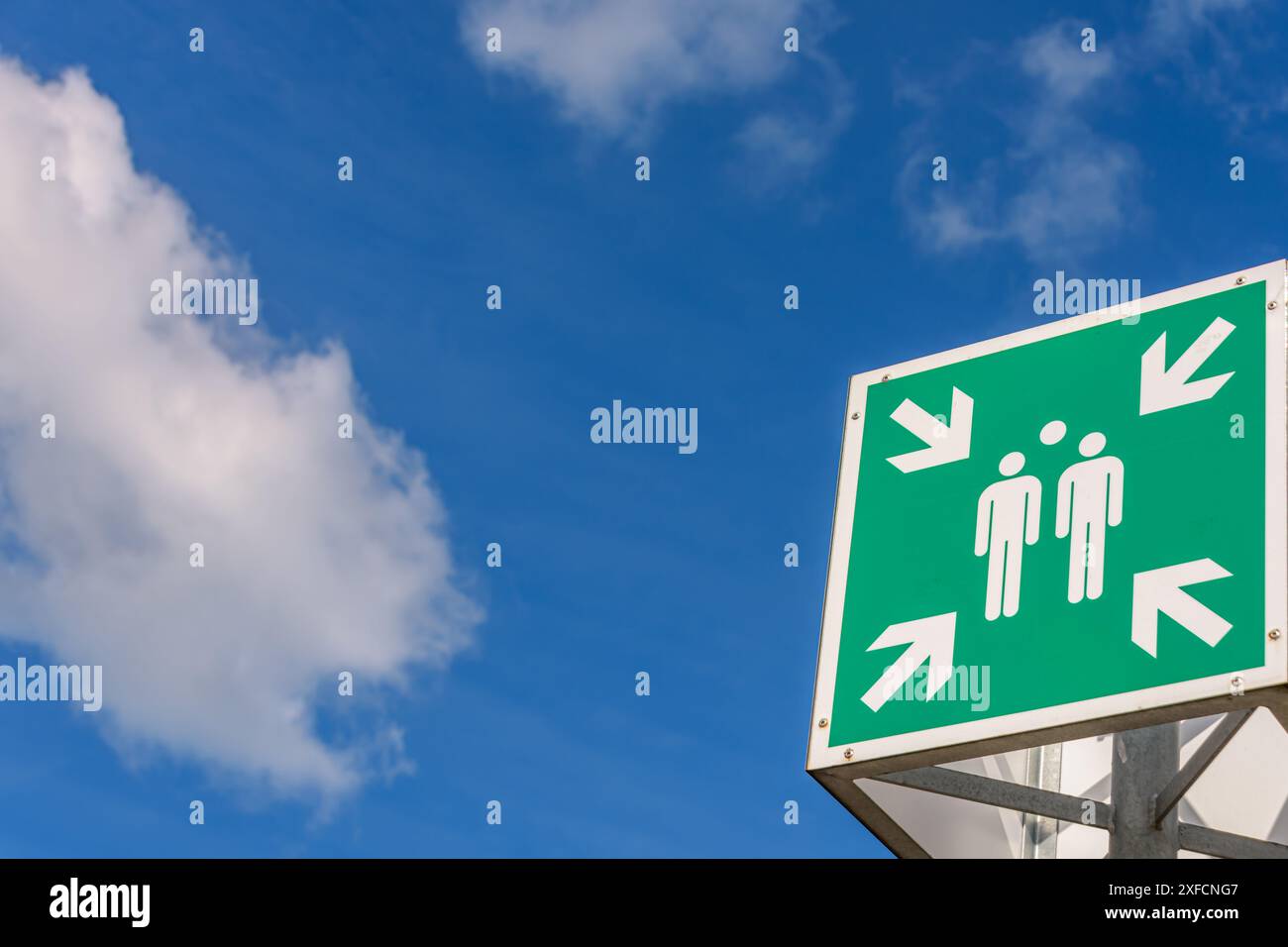 green sign for assembly point against a blue sky with clouds in the ...