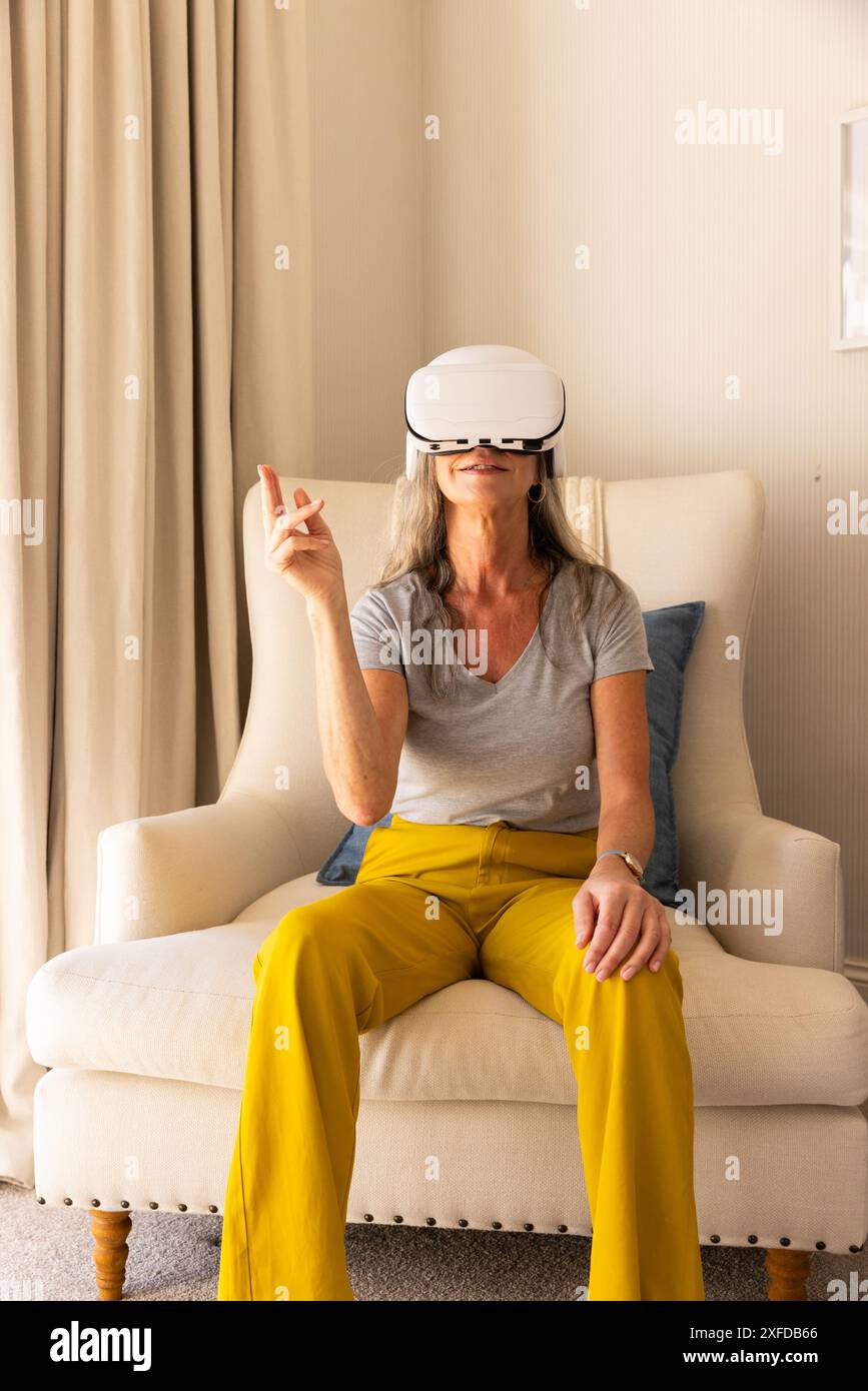 Using VR headset, mature woman sitting on chair interacting with ...