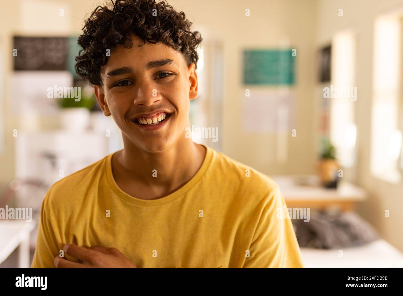 Smiling teenage boy in high school classroom, wearing yellow shirt and ...