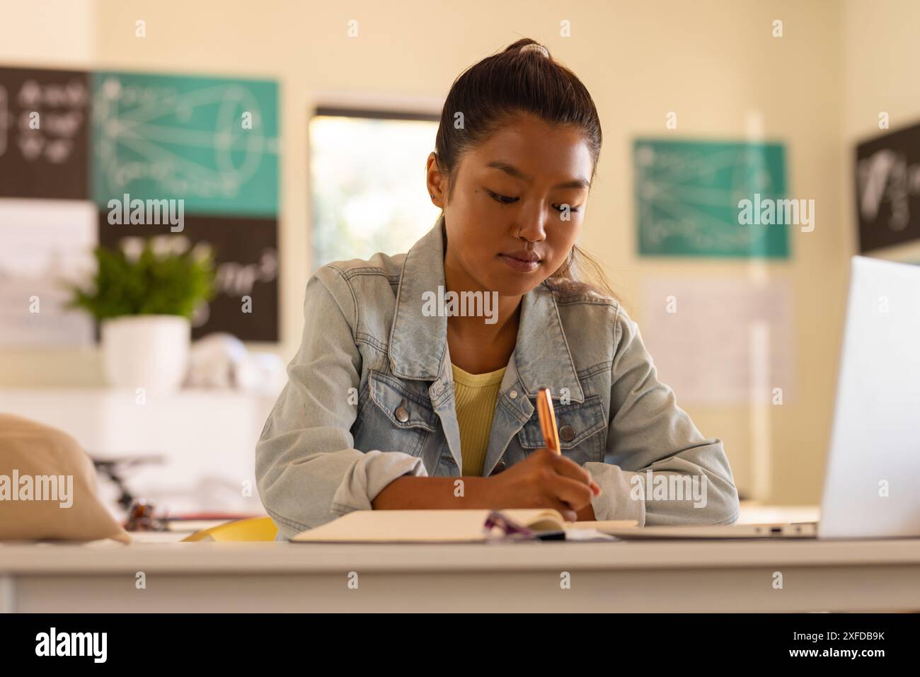 In high school, teenage girl writing in notebook while studying at desk ...