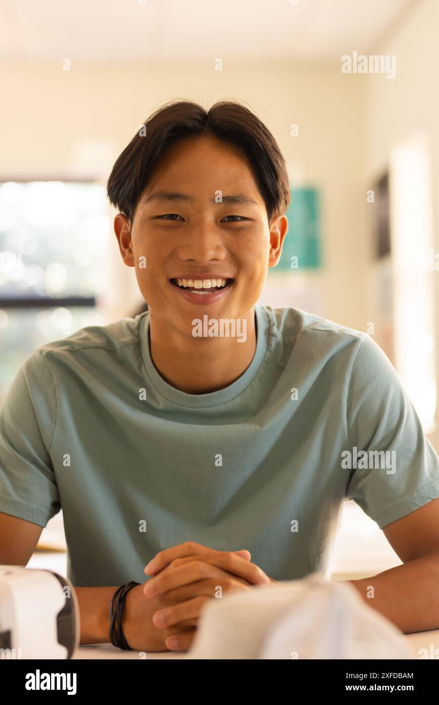Smiling teenage boy sitting at high school desk, looking at camera in ...