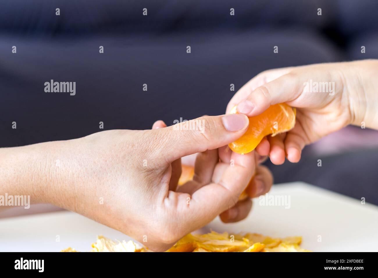 Adult's hand offering tangerine to a child Stock Photo - Alamy