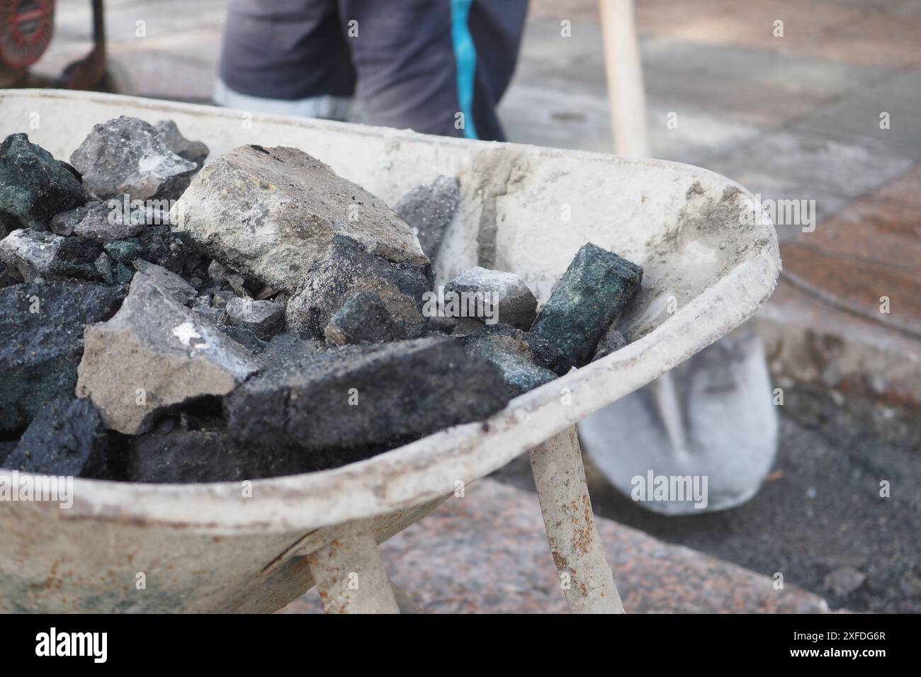 Wheelbarrow with materials on worksite, worker unloading rocks and ...