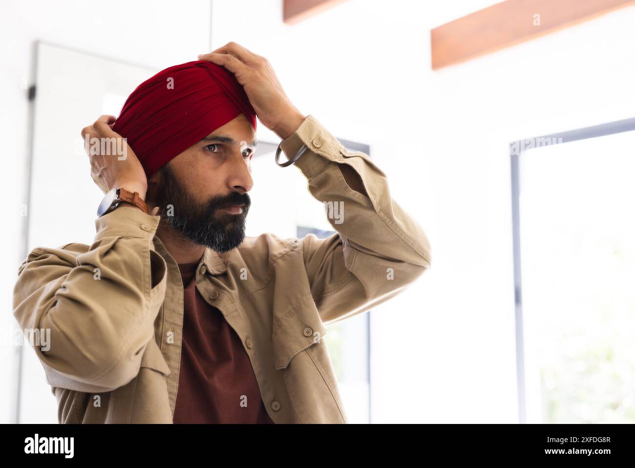 Adjusting red turban, man standing indoors, focusing on traditional ...