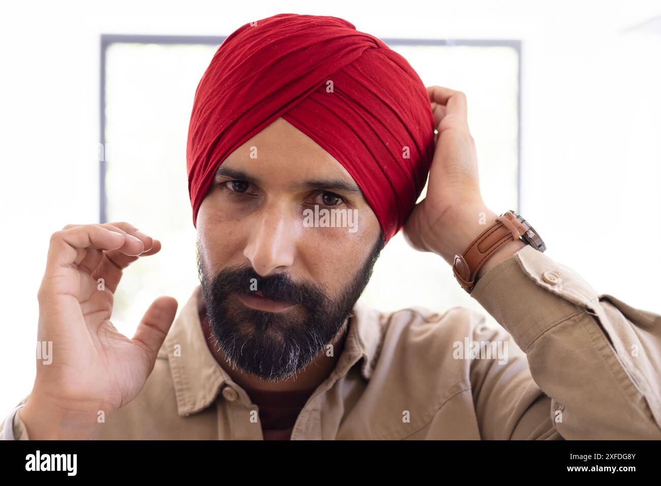 Adjusting red turban, man with beard looking confidently at camera ...