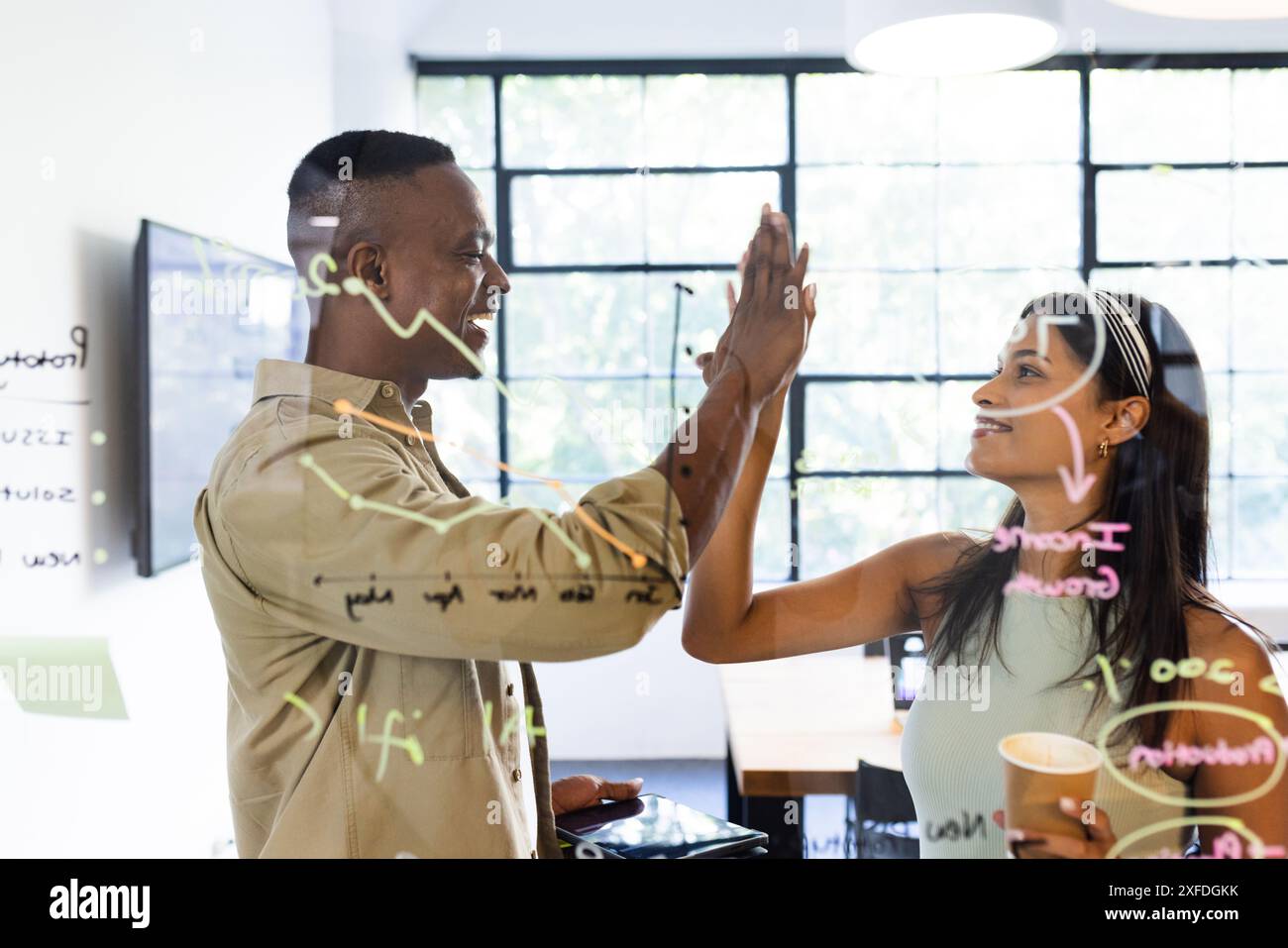 High-fiving, colleagues celebrating success in modern office with glass ...