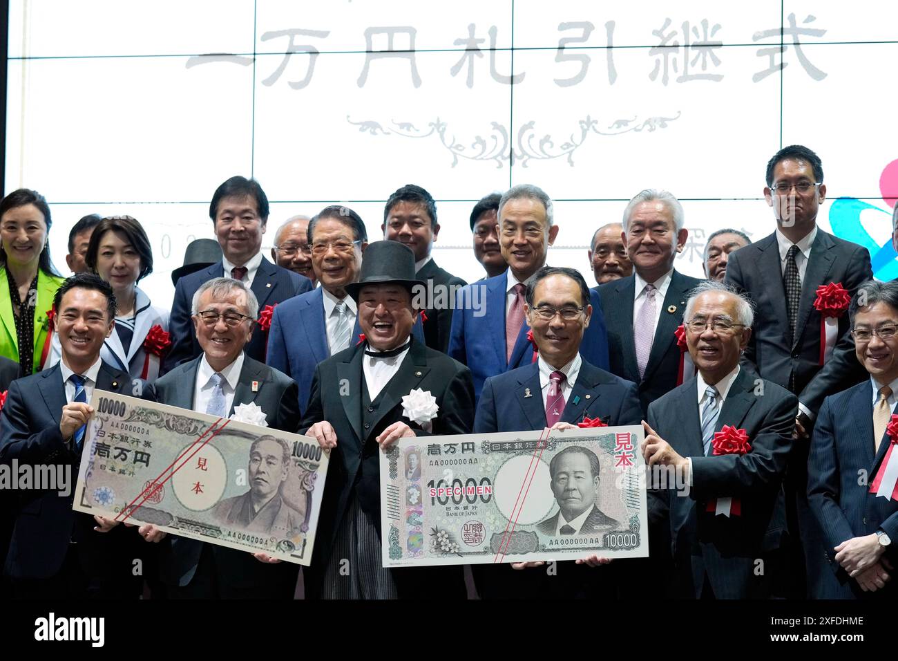 Officials pose with enlarged copies of the new and old 10000 yen ...