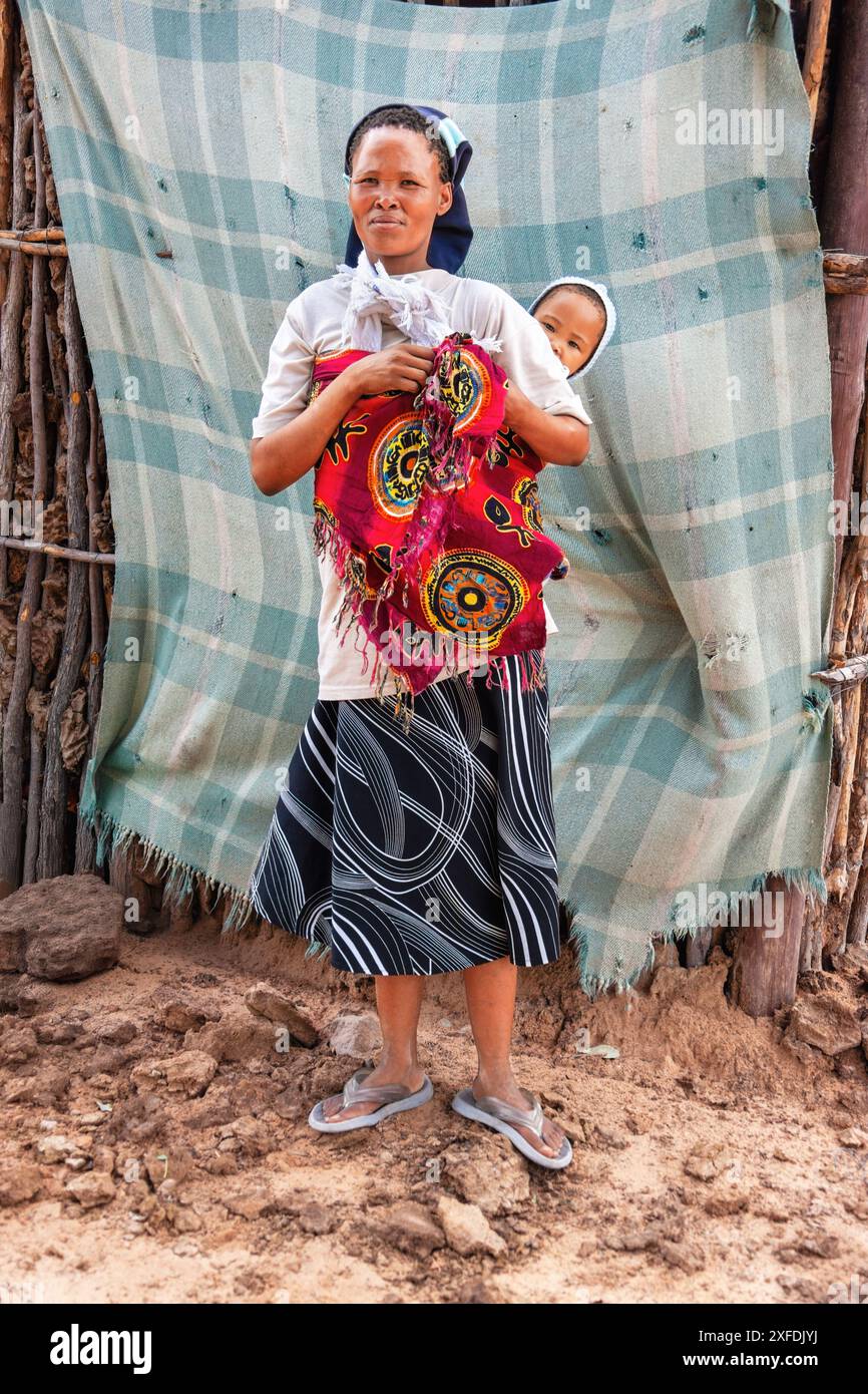 african woman carry child in the back traditional way, mud house in the ...