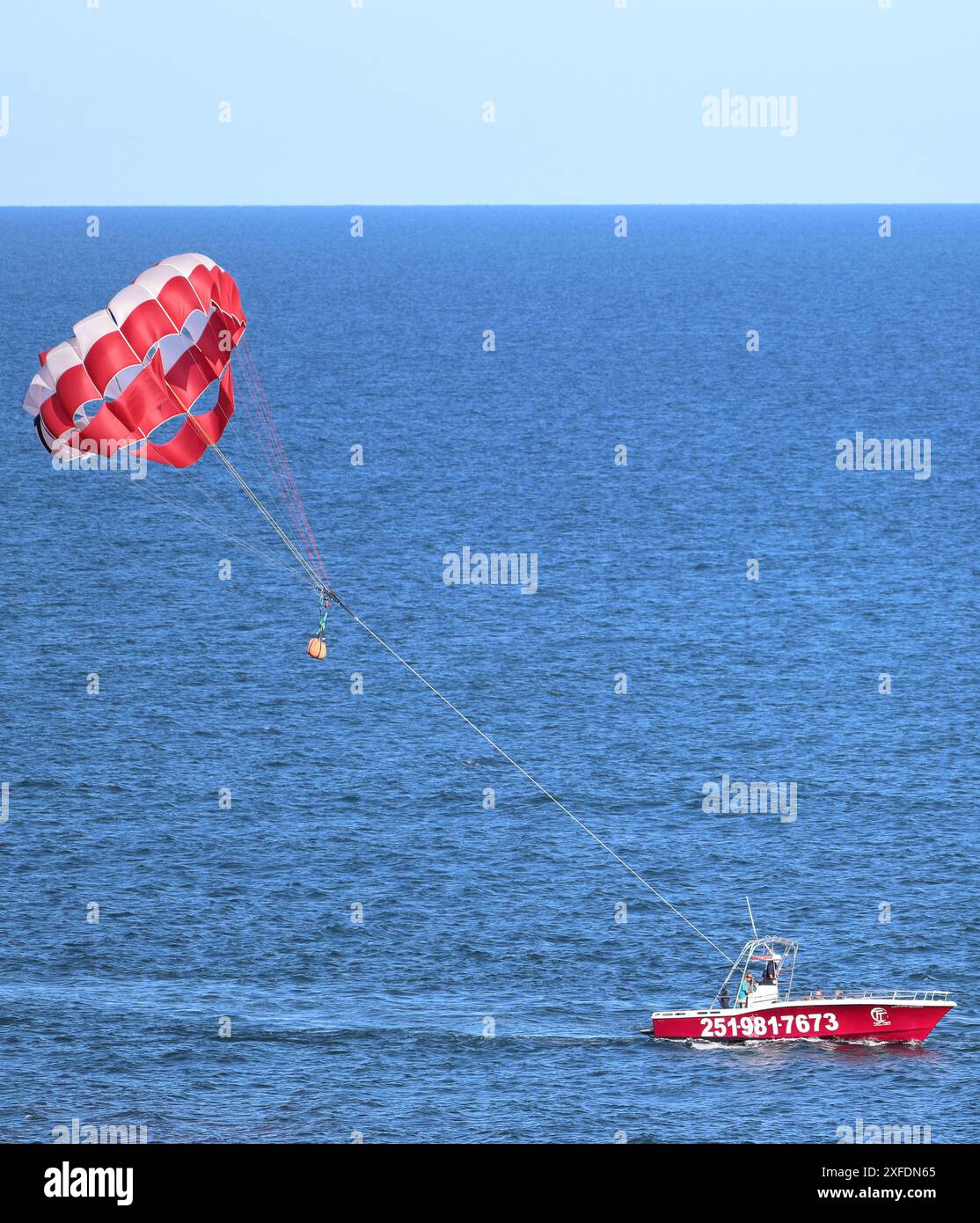 Boat pulling a parasail across sky over ocean Stock Photo - Alamy