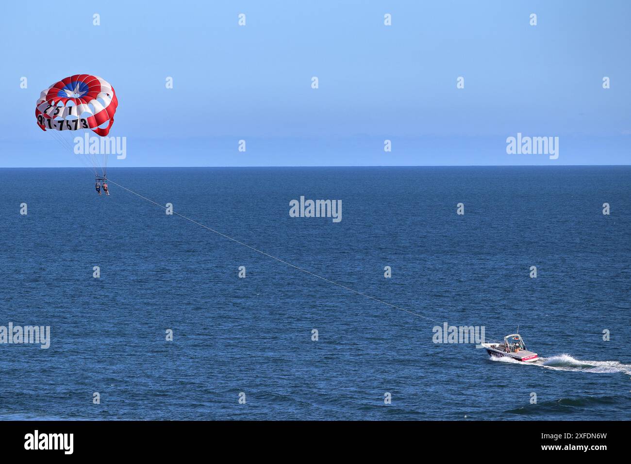 Boat pulling a parasail across sky over ocean Stock Photo - Alamy