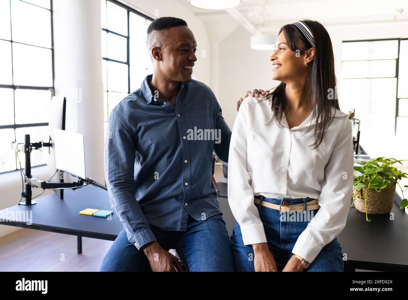 Smiling colleagues sitting on desk in modern office, enjoying ...