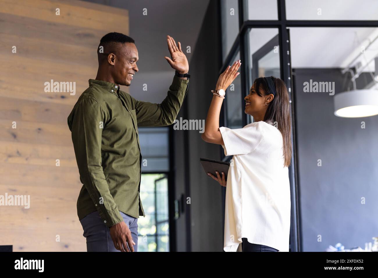 Celebrating success, colleagues high-fiving in modern office ...
