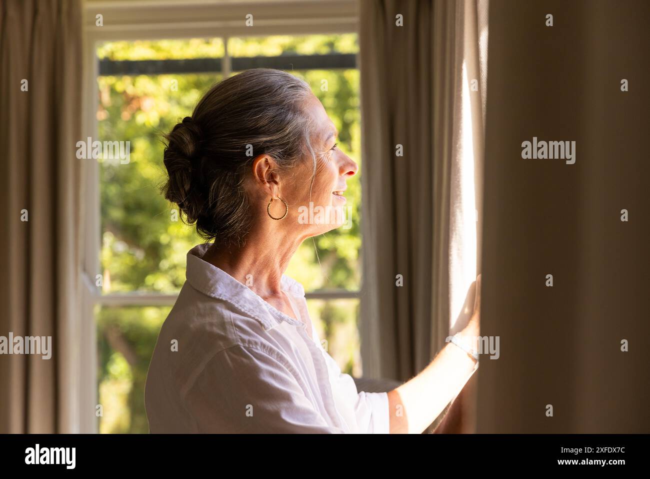 Enjoying sunlight, mature woman looking out window at home Stock Photo ...