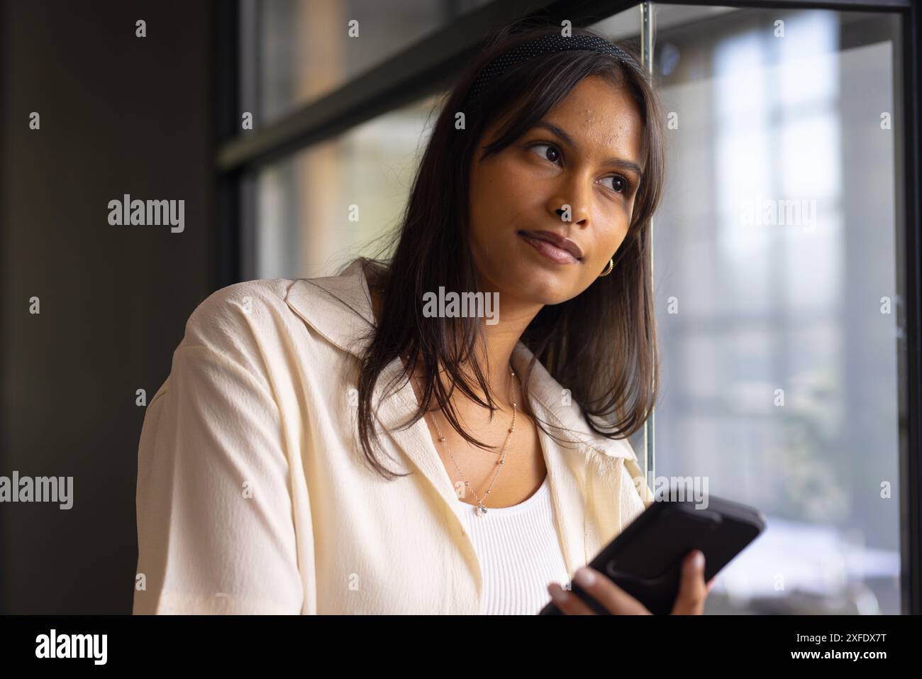 Holding smartphone, businesswoman leaning on window, thinking in modern ...