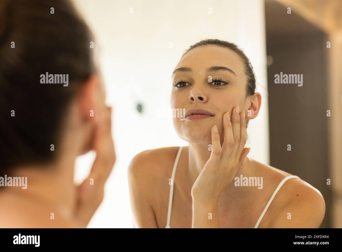 Young woman examining her face in mirror, focusing on skincare routine ...