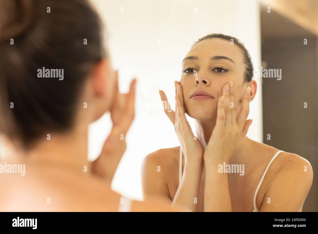 Applying skincare, woman looking at reflection in bathroom mirror ...