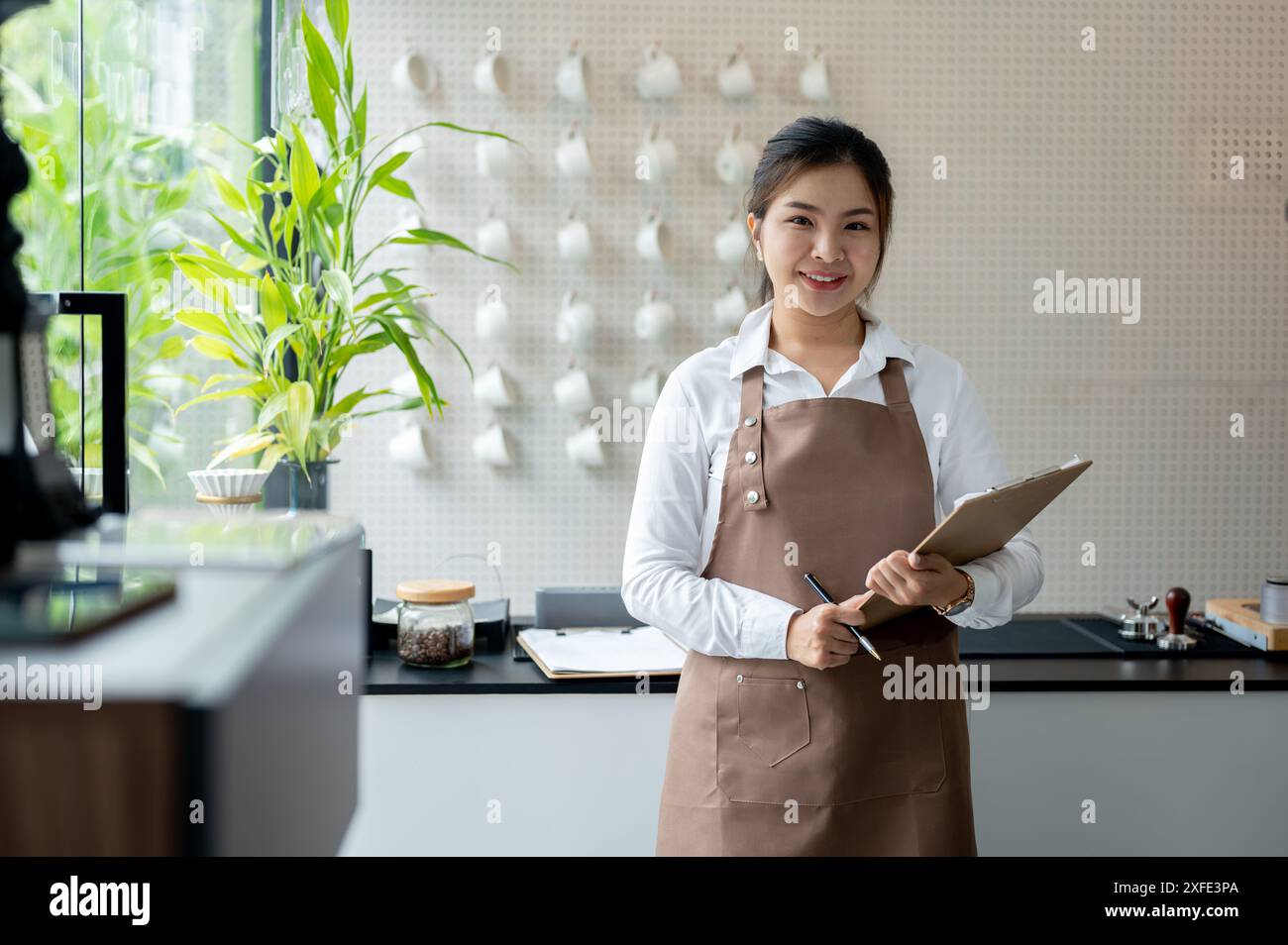 A charming, smiling young Asian female server or barista in a brown ...