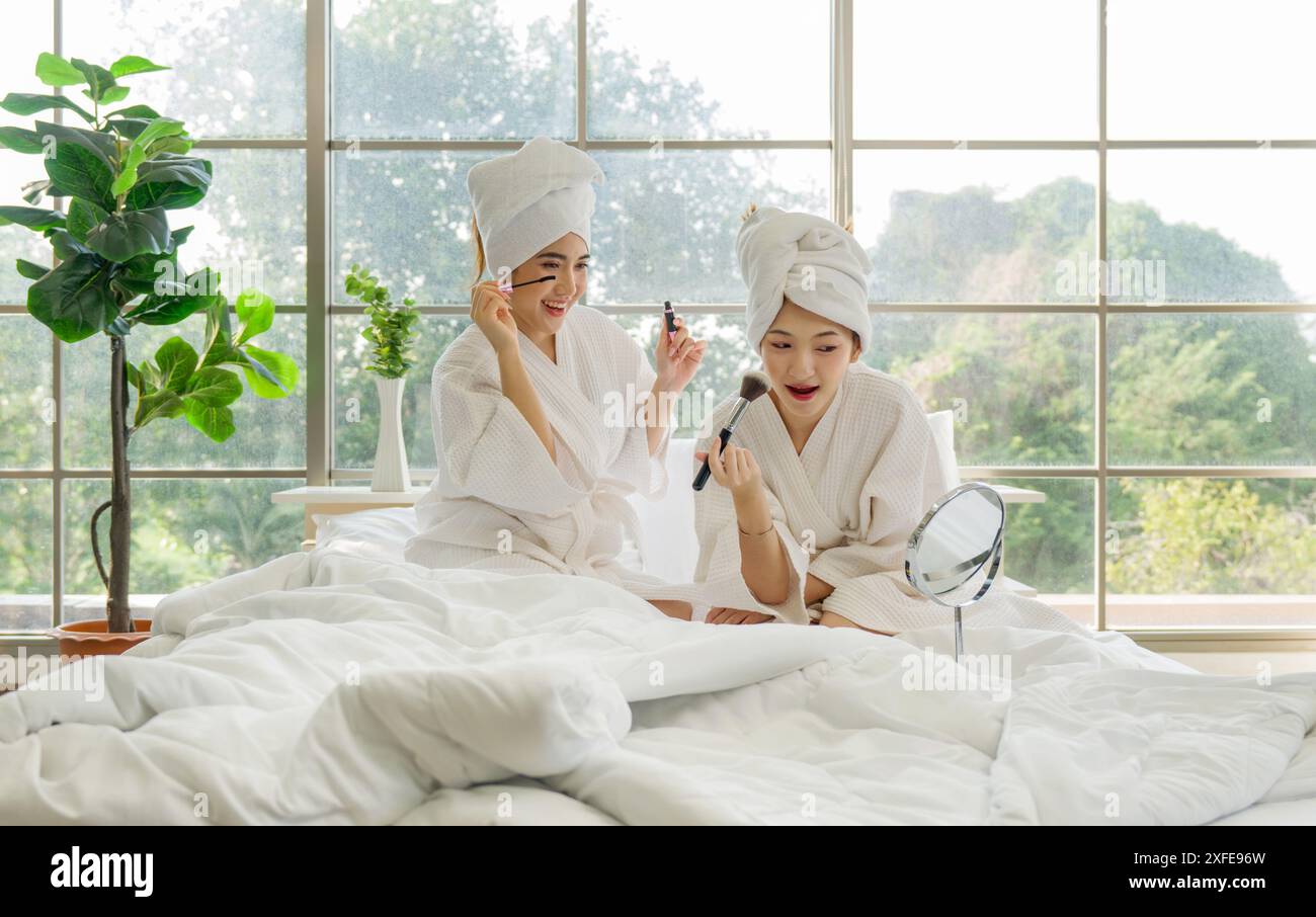 Two asian women are sitting relax on a bed in white robe and towel ...