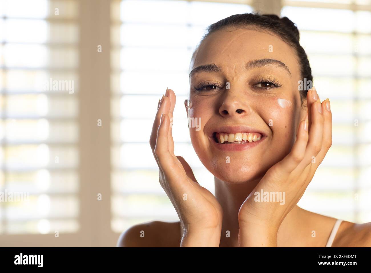 Applying moisturizer, young woman smiling and enjoying skincare routine ...