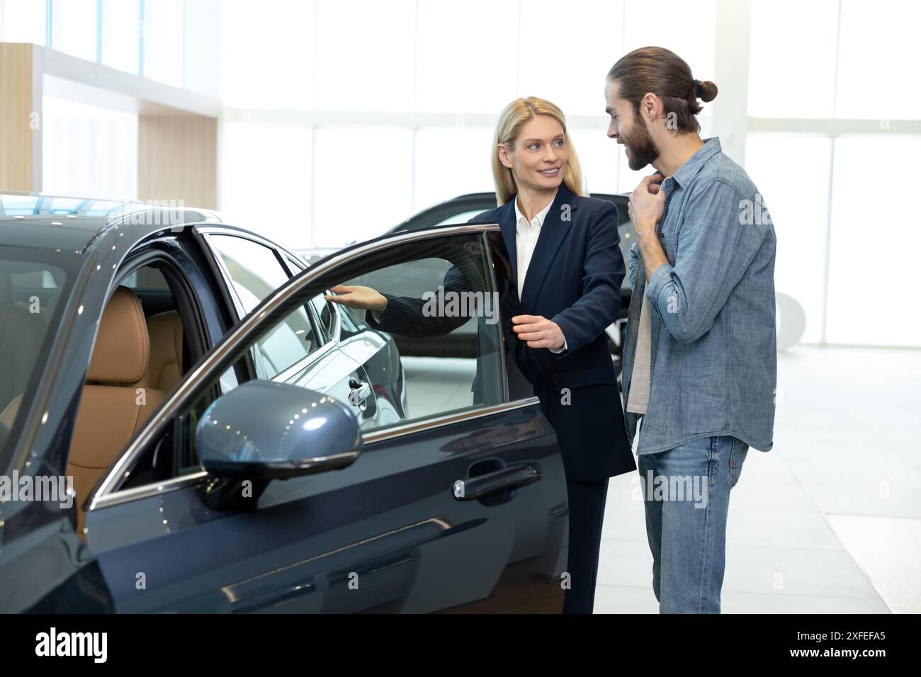 Female sale assistant in a dealership showing a new car to the customer ...