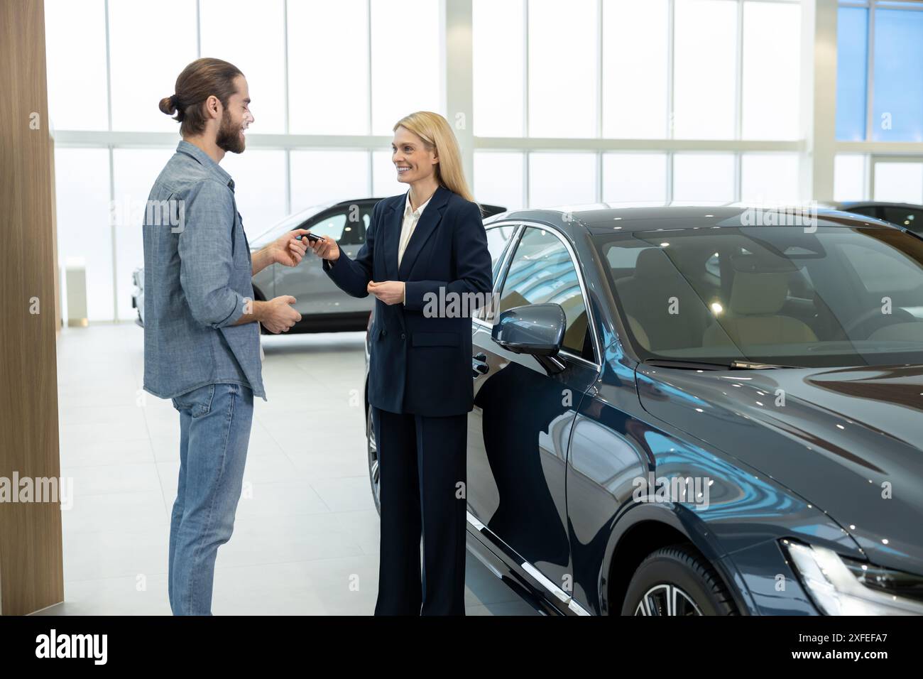 Female sale assistant in a dealership showing a new car to the customer ...