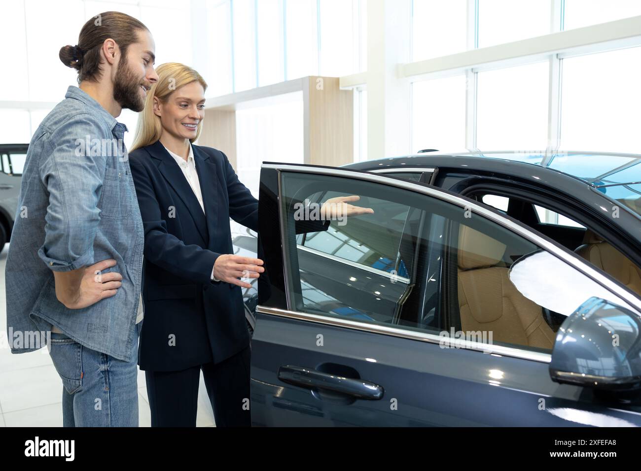 Female sale assistant in a dealership showing a new car to the customer ...