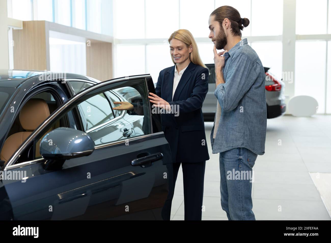 Female sale assistant in a dealership showing a new car to the customer ...
