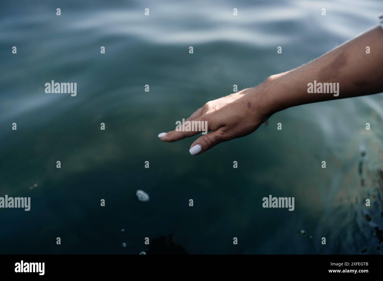 The hand touches the water, creating ripples. The water is calm and ...