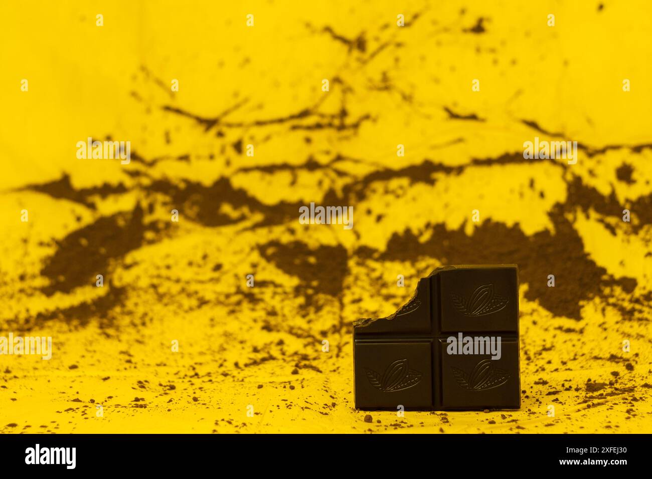 Bitten chocolate bar and scattered cocoa powder on crumpled yellow ...