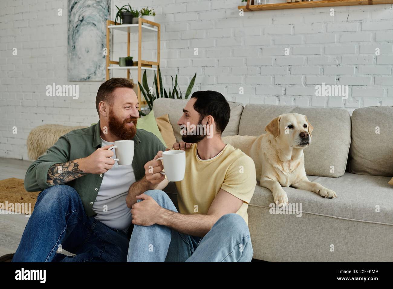 Two men, a bearded gay couple, are sitting on a couch cups near ...