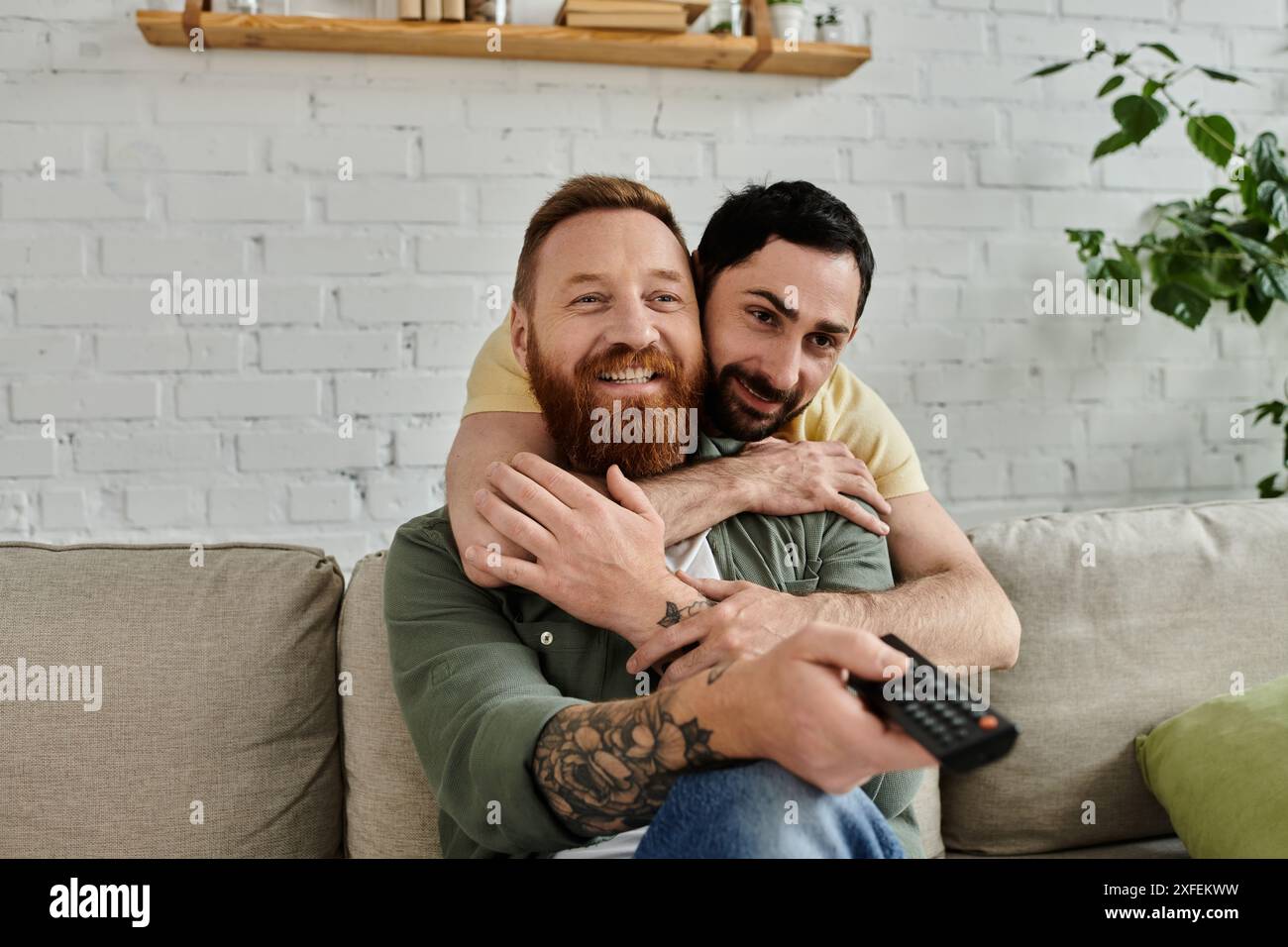 Bearded Gay Couple Sharing A Warm Hug While Seated On A Cozy Couch In The Living Room Stock