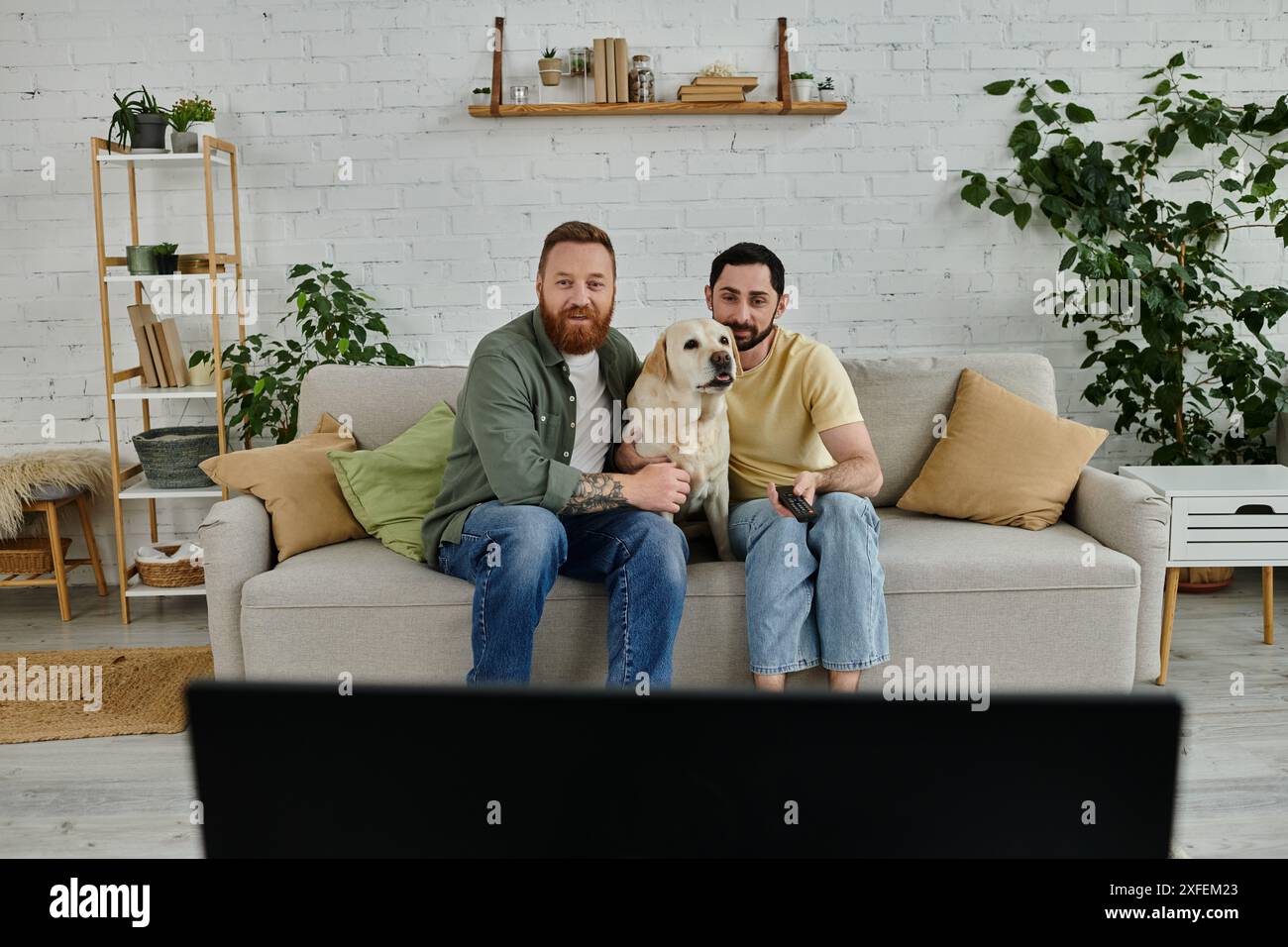 Two Men A Bearded Gay Couple Sit Contentedly On A Couch With Their Labrador Retriever In A