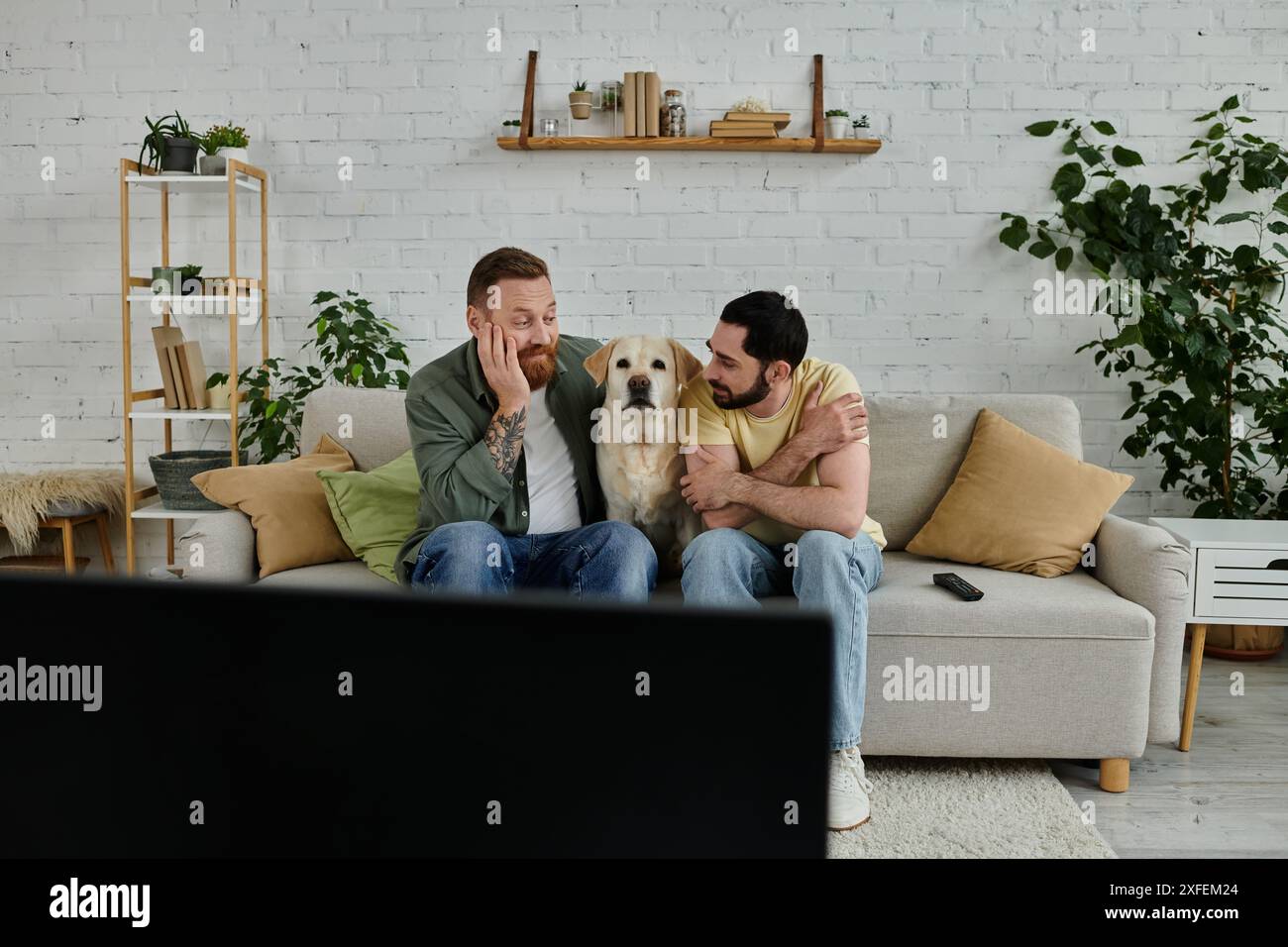 Two bearded men sit on a couch, cuddling with their labrador in a cozy ...