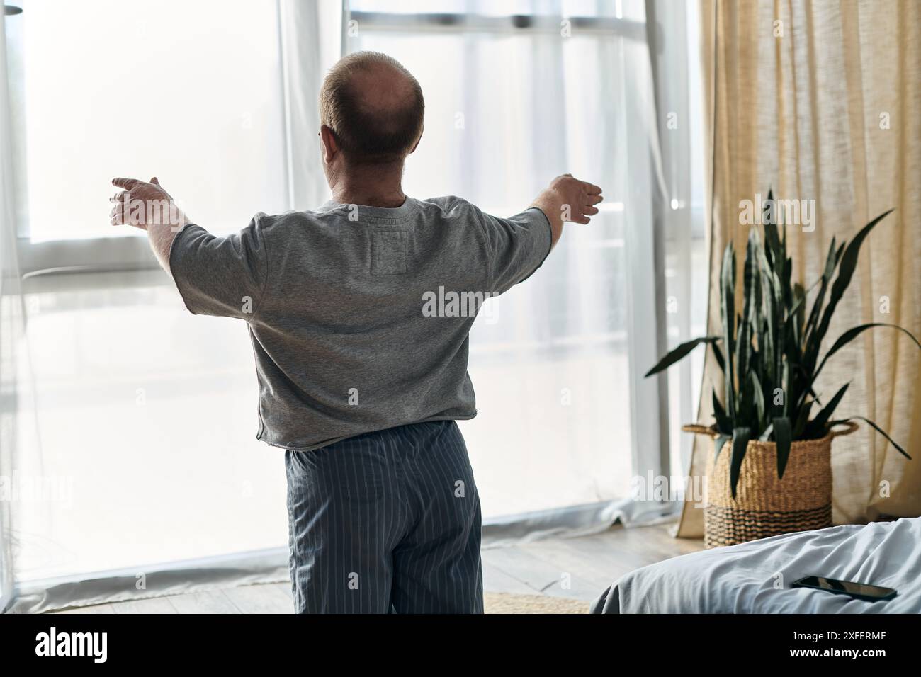 A man with inclusivity stretches in front of a window, arms ...
