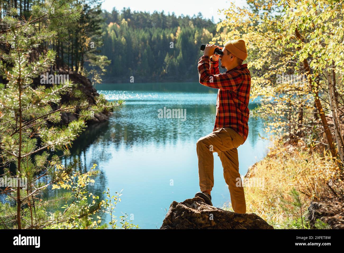 Young man looking through binoculars at birds on lake in fall ...