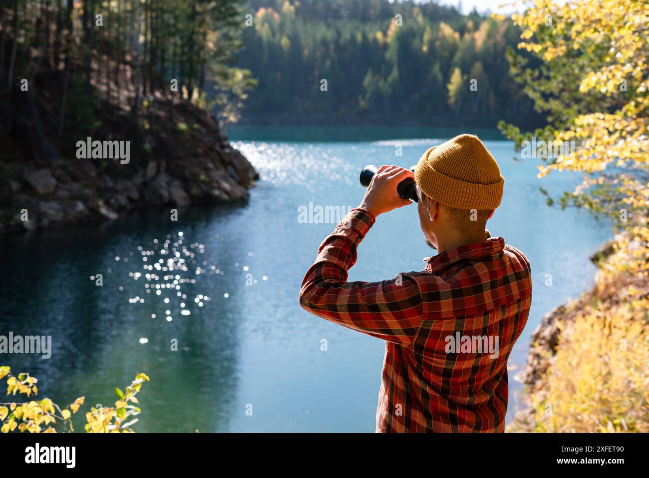 rear view of man looking through binoculars at birds on lake in fall ...