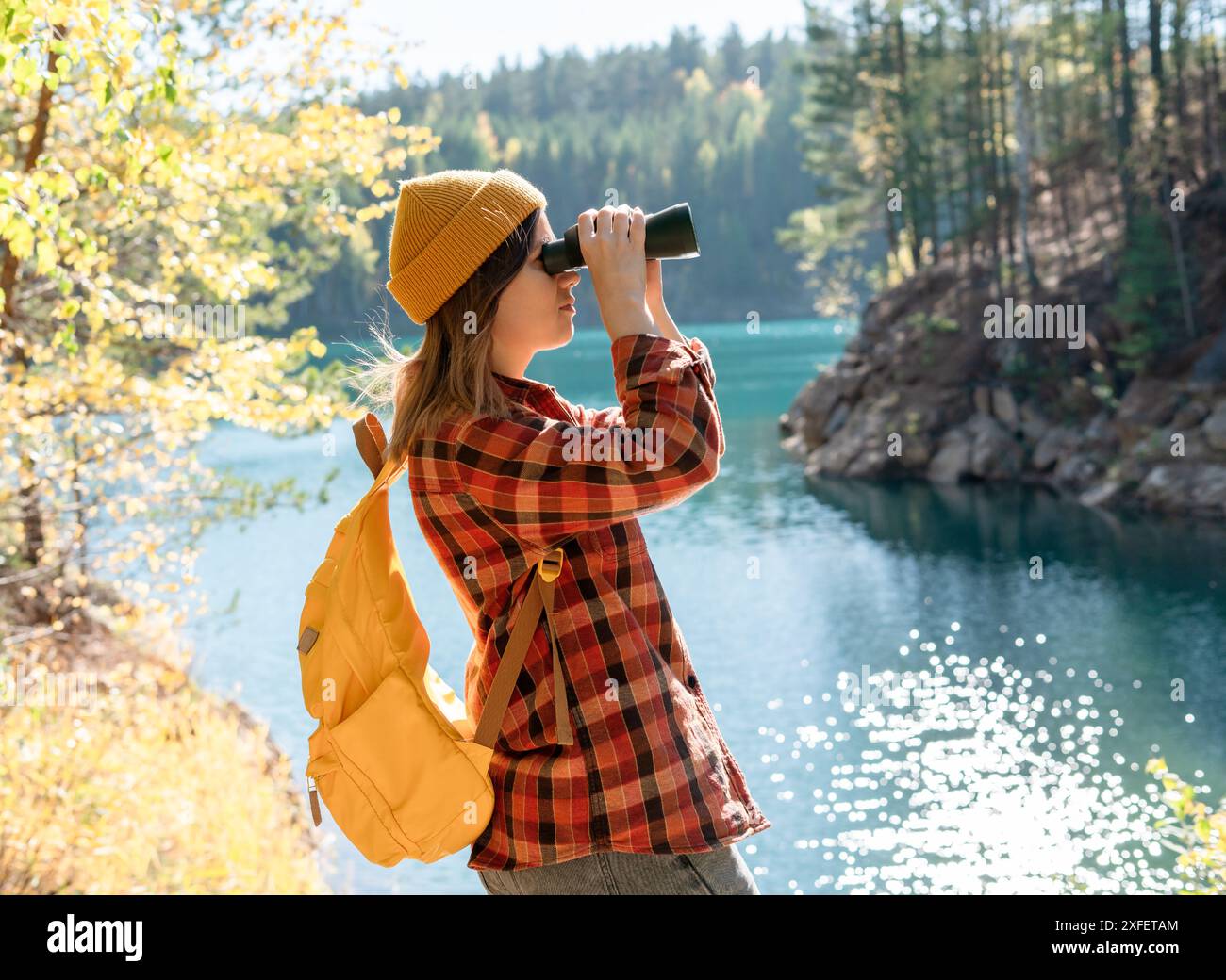 Young millennial woman with yellow backpack holding binoculars ...
