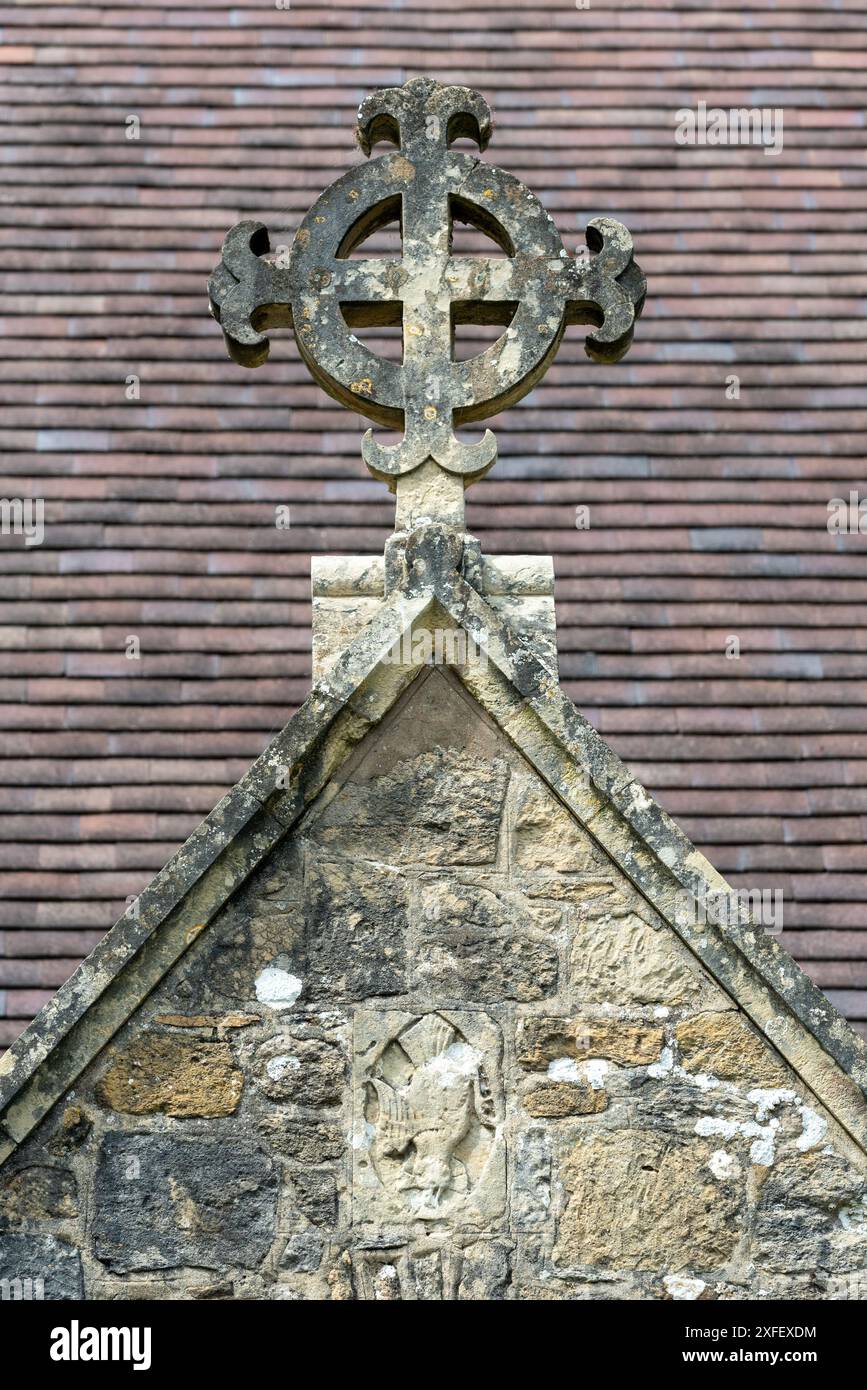 Stone cross above a church entrance with out of focus roof tiles behind ...