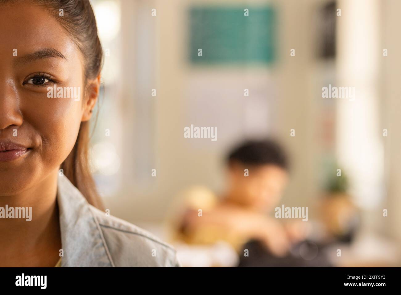 Smiling teenage girl in high school classroom with blurred student in ...